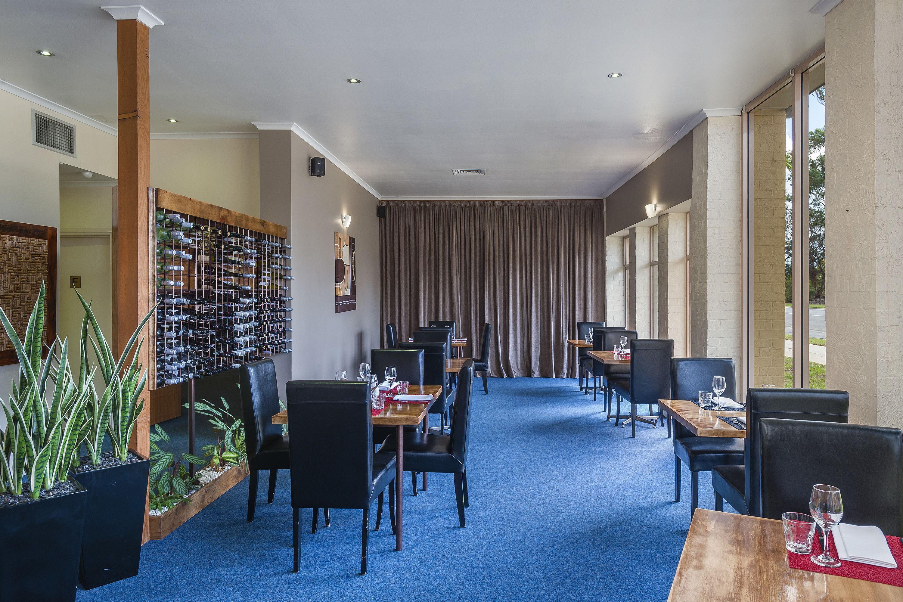 Espaço de refeições de hotel com mesas, cadeiras e uma parede de garrafas de vinho.