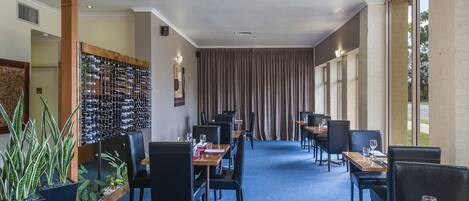 Espaço de refeições de hotel com mesas, cadeiras e uma parede de garrafas de vinho.