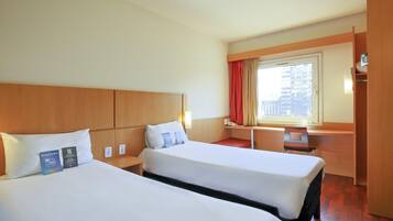 Quarto de hotel com duas camas, uma escrivaninha e uma janela com cortinas.
