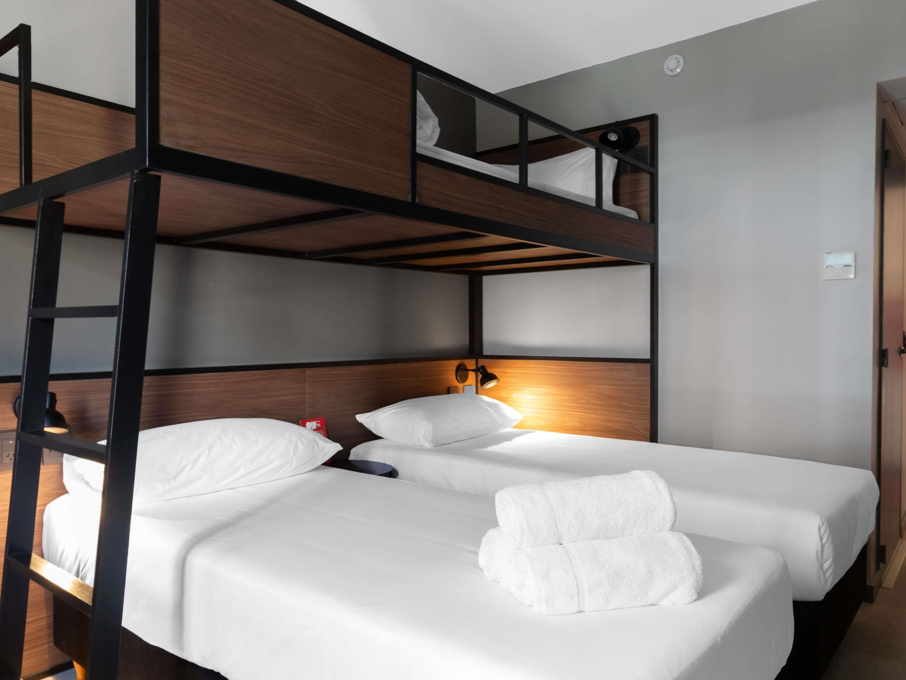 Quarto com beliche, cabeceira de madeira, duas camas, escada e luminária de cabeceira.
