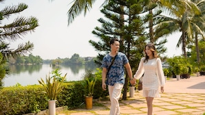 Um casal caminhando por um caminho pavimentado, com um lago e palmeiras ao fundo.