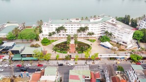 Um hotel grande com um pátio central, cercado por palmeiras e um corpo de água.