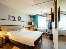 Quarto de hotel com uma cama grande, uma mesa com um laptop, uma televisão e um guarda-roupa.