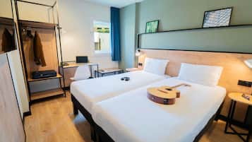Quarto de hotel com duas camas, uma escrivaninha com um laptop, uma guitarra em uma das camas e um cabideiro.