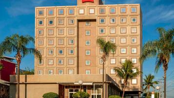 Um hotel com vários andares e um sinal vermelho chamativo da marca 'ibis', apresentando uma fachada simétrica com janelas uniformemente distribuídas e uma entrada central.