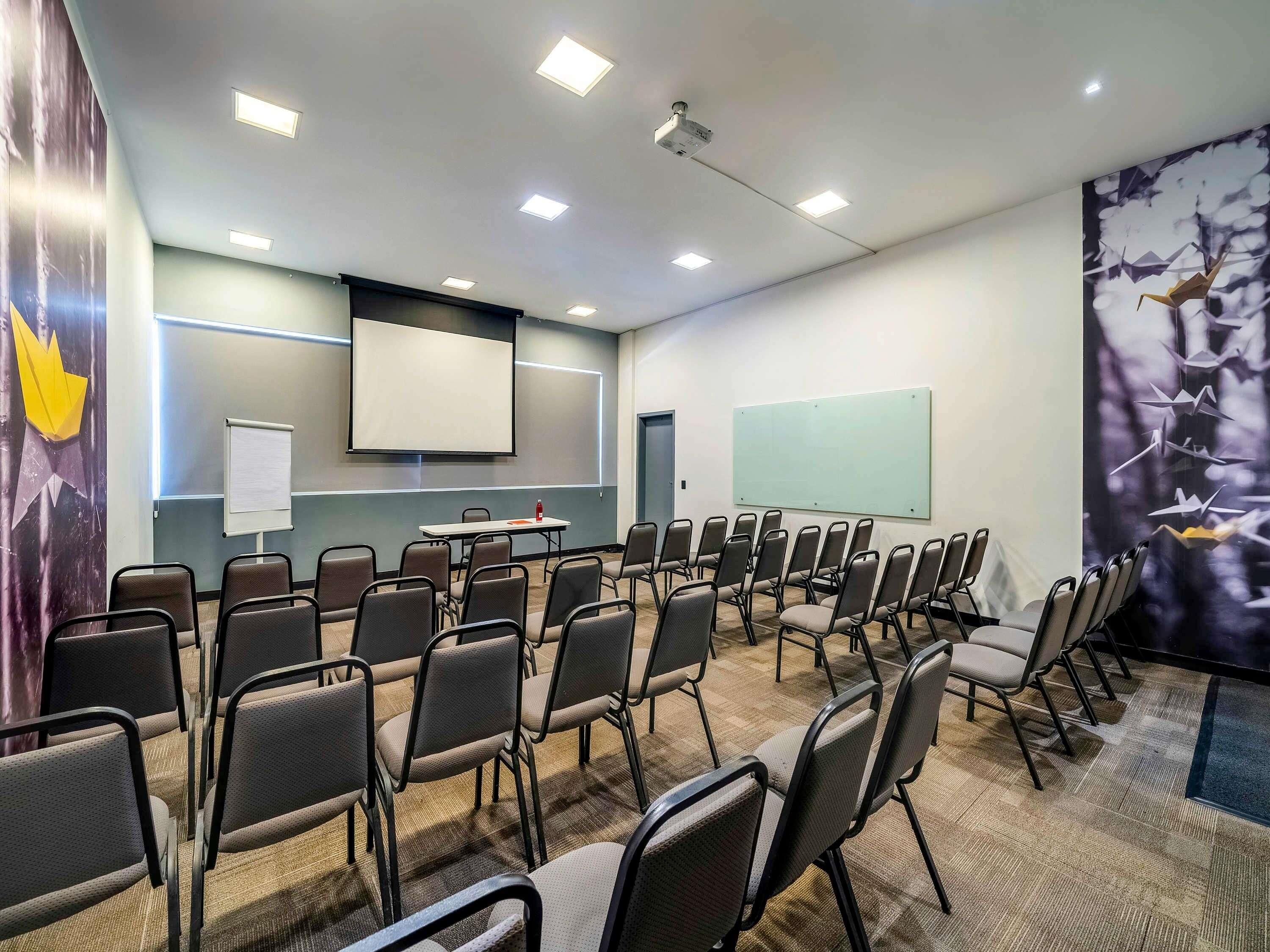 Uma sala de conferências com fileiras de cadeiras, um projetor e um quadro branco.