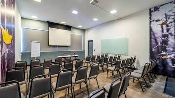 Uma sala de conferências com fileiras de cadeiras, um projetor e um quadro branco.