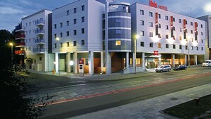 Um hotel moderno com um letreiro grande 'ibis HOTEL', vários andares e uma área de estacionamento com carros.