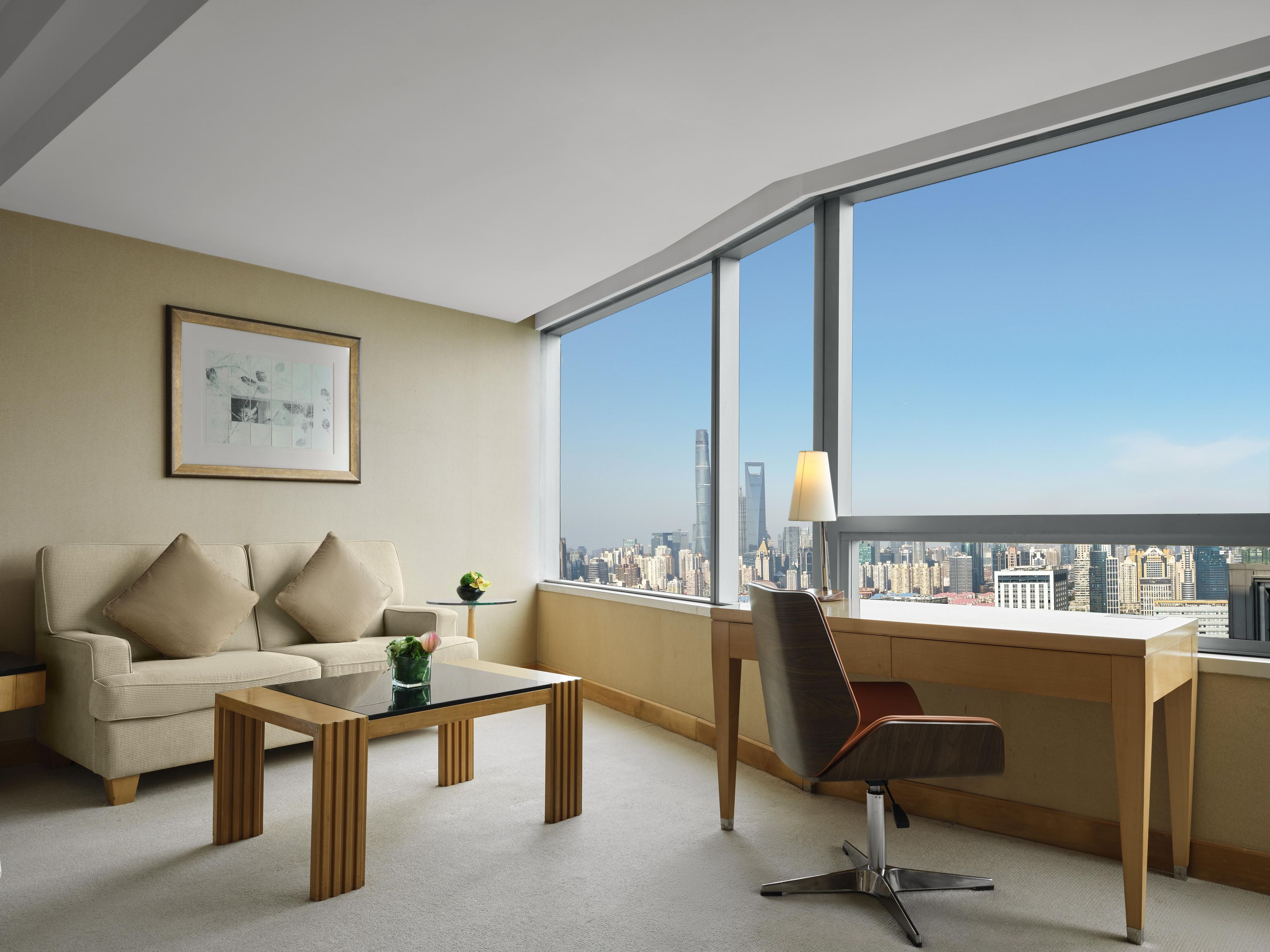 Quarto de hotel moderno com vista para a cidade, um sofá, uma mesa de centro e uma escrivaninha com cadeira.