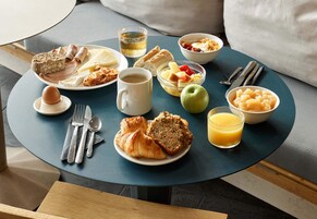Uma mesa de café da manhã com croissants, queijo, presunto, frutas e suco.