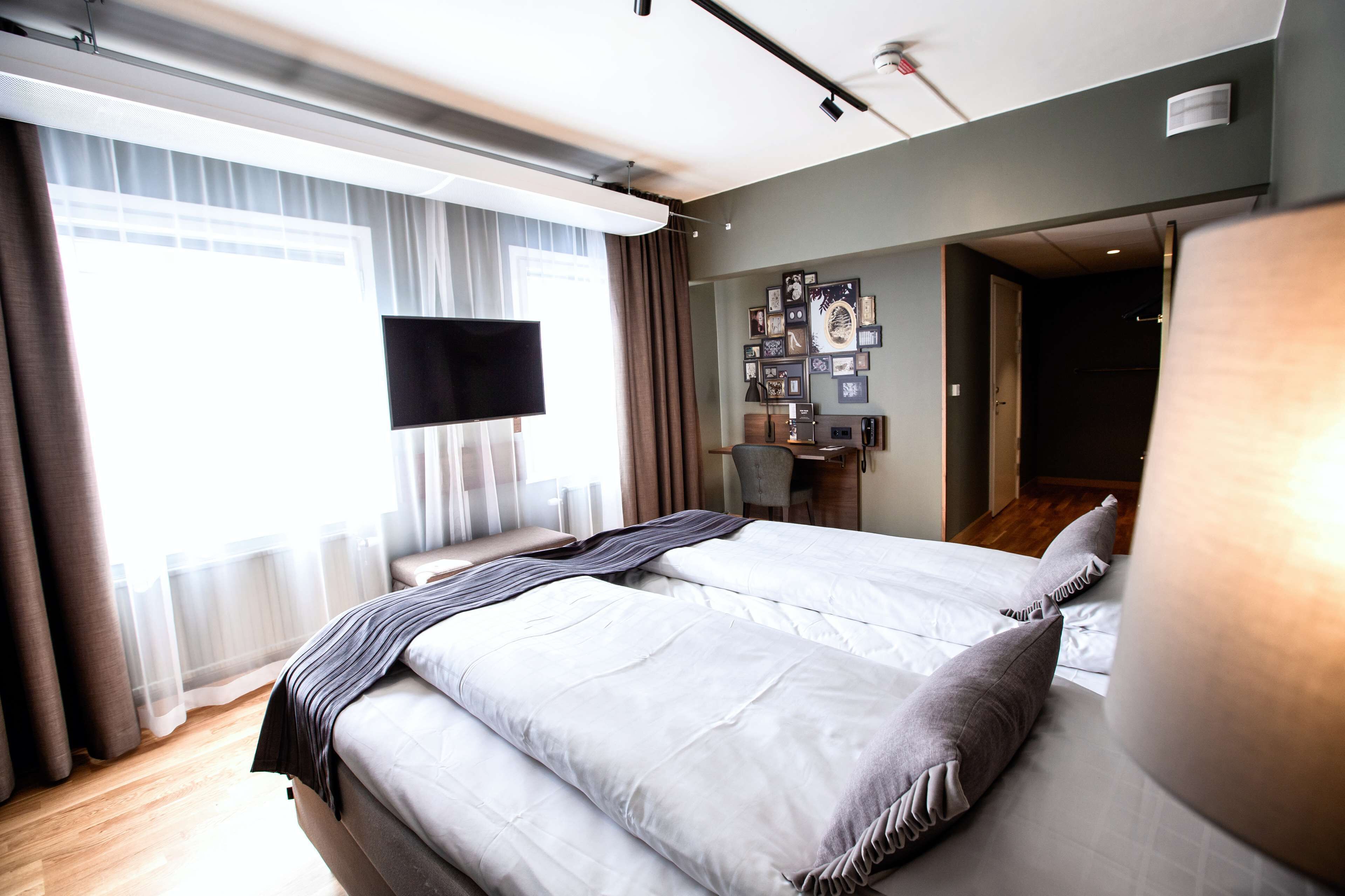 Quarto de hotel moderno com uma cama grande, televisão de tela plana, painel de fotos na parede e piso de madeira.