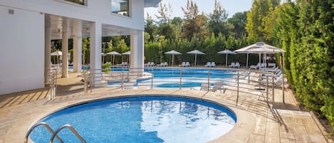 Um hotel moderno com uma grande piscina ao ar livre, espreguiçadeiras e guarda-sóis.