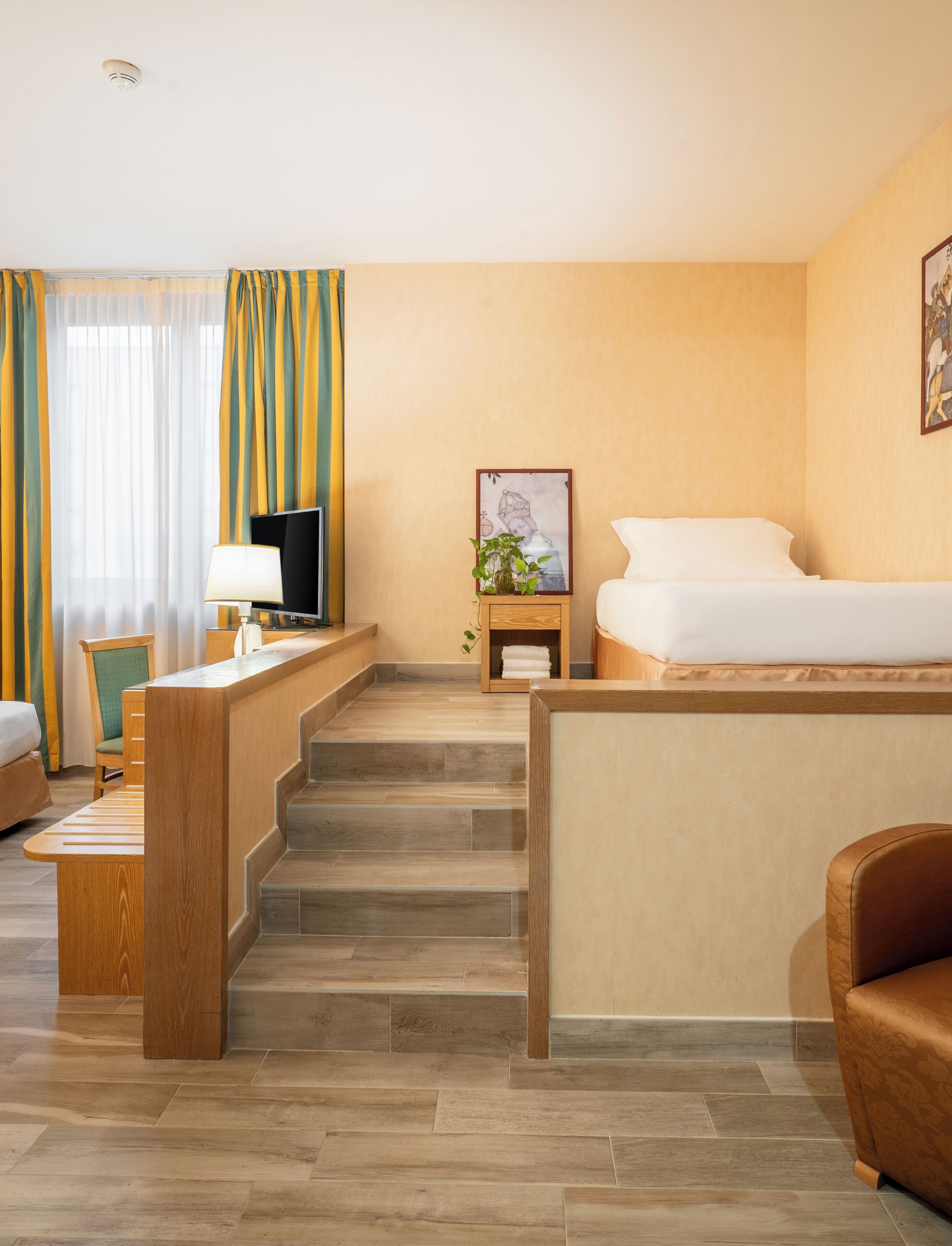 Quarto de hotel com cama, escrivaninha, cadeira, televisão e escada.