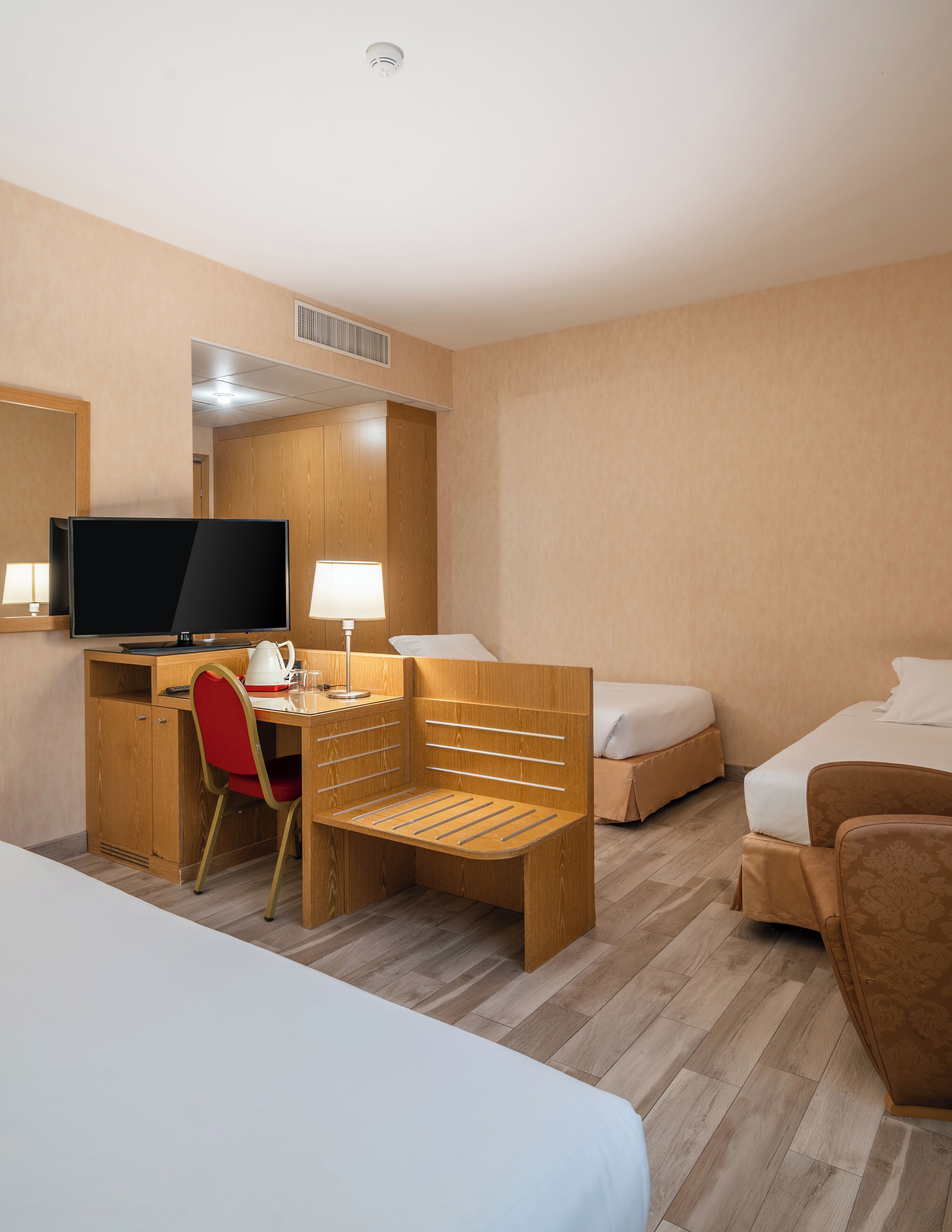 Quarto de hotel com cama, escrivaninha, cadeira, televisão e luminária.