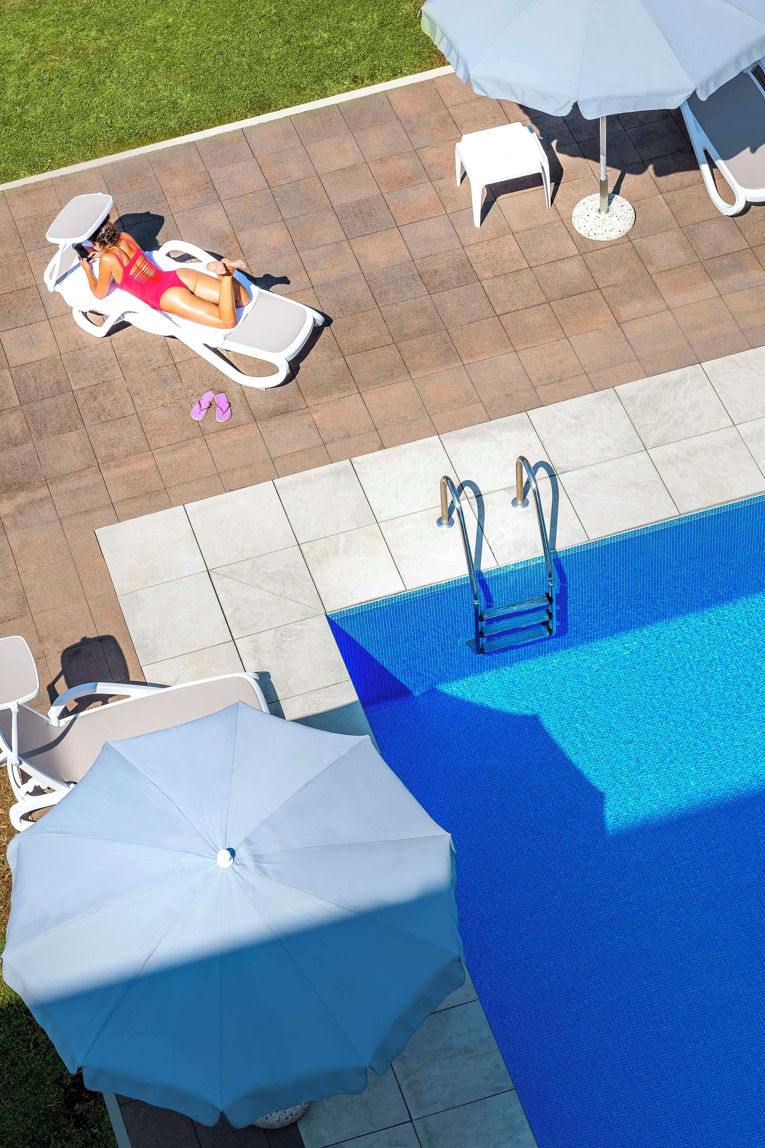 Uma área de piscina com espreguiçadeiras, guarda-sol e escada de acesso.