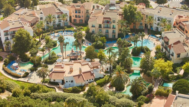 Resort com várias piscinas, palmeiras e diferentes estilos de construção.