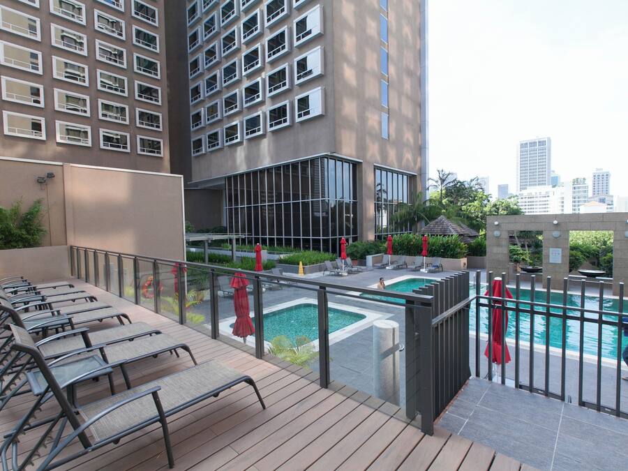 Área de piscina no terraço, com espreguiçadeiras e guarda-sóis, cercada por um parapeito de vidro.