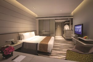 Quarto de hotel com cama, escrivaninha, cadeira, televisão e uma fruteira pequena.