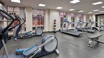 Uma academia com várias esteiras e equipamentos elípticos, janelas amplas e um design moderno e limpo.