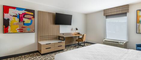 Quarto de hotel com cama, escrivaninha, cadeira, televisão e obras de arte nas paredes.
