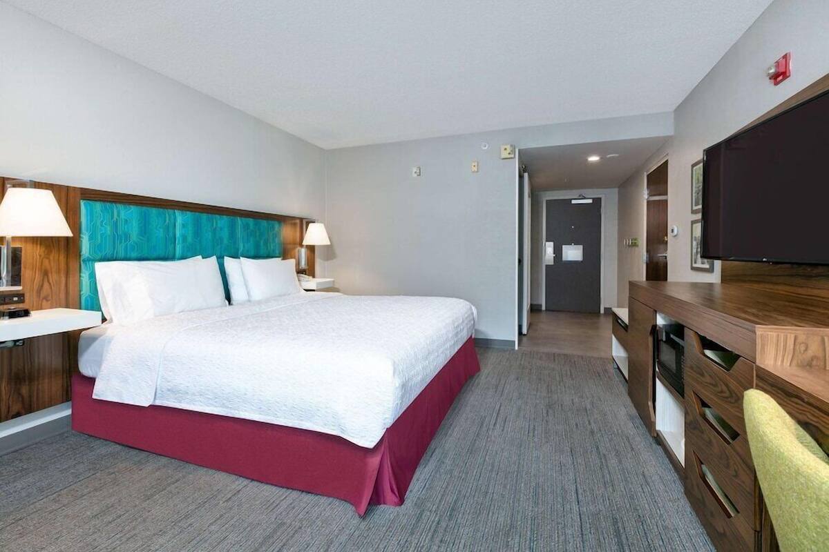 Quarto de hotel com cama, mesas de cabeceira, escrivaninha e televisão.
