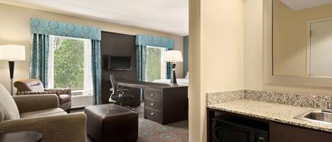 Quarto de hotel com sofá, escrivaninha, cadeira, televisão, micro-ondas e pia.