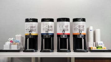 Quatro dispensadores de café com as indicações 'Torra Clara', 'Torra Escura', 'Água Quente' e 'Descafeinado' em uma bancada com guardanapos e caixas de chá.