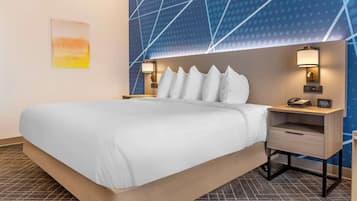Quarto de hotel com uma cama grande, uma mesa de cabeceira com abajur e uma parede com padrão geométrico.