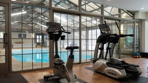 Ginásio interior com duas bicicletas de exercício e vista para uma piscina interior através de grandes janelas.
