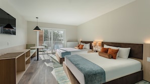 Quarto de hotel moderno com uma cama grande, mesas de cabeceira, uma escrivaninha e uma janela com persianas.