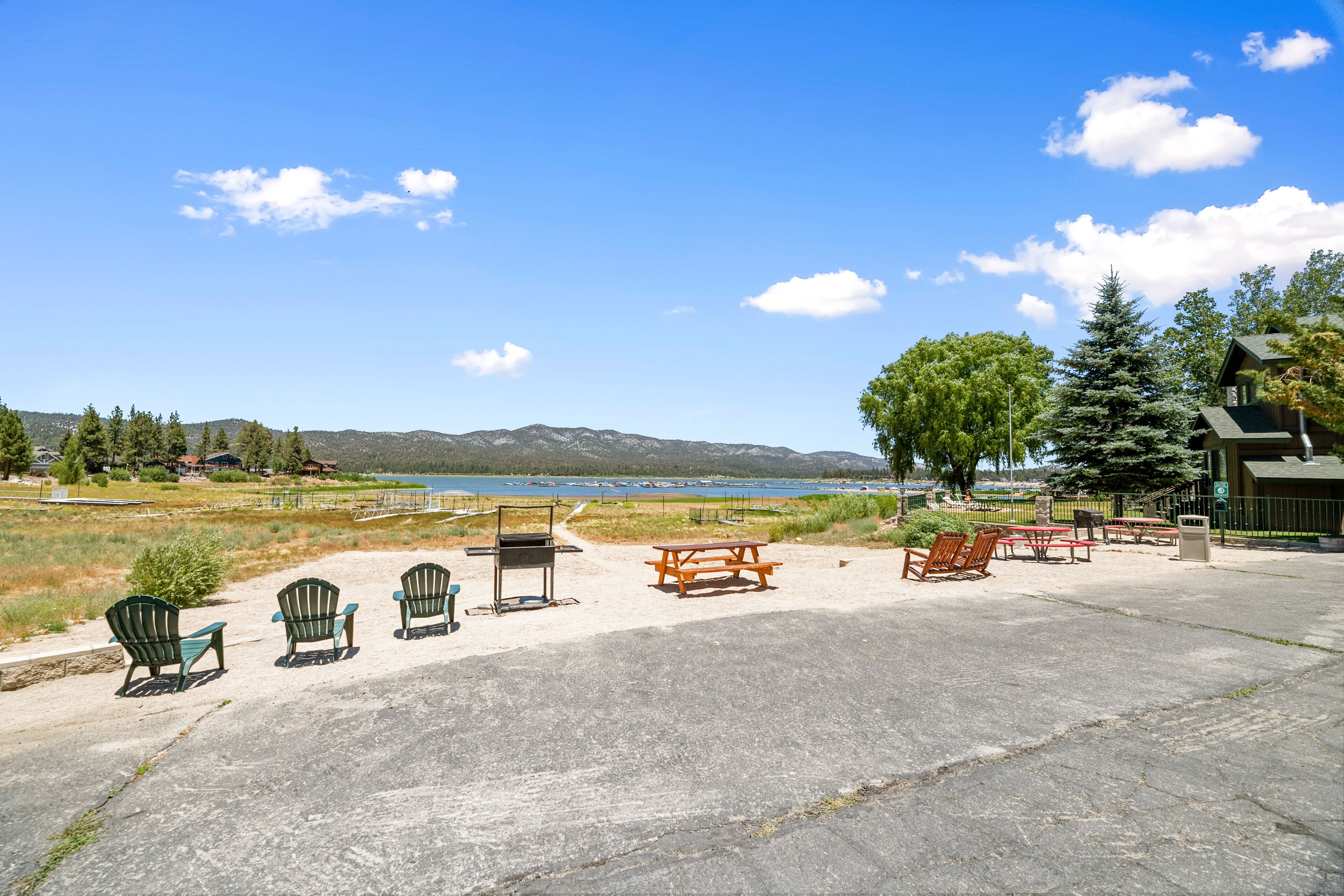 Uma área para piquenique à beira do lago, com cadeiras Adirondack, mesa de piquenique e vista para o lago e montanhas.