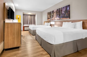 Quarto de hotel com duas camas, televisão, escrivaninha, janela com cortinas e uma pintura com vista para a cidade.