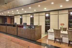 Uma receção com design moderno, balcão de check-in e zona de espera com cadeiras e mesa.