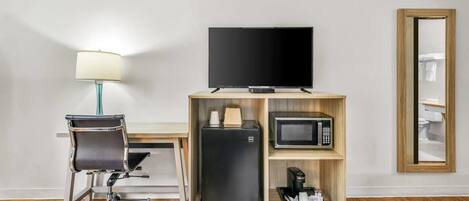 Quarto de hotel com escrivaninha, cadeira, televisão, micro-ondas, frigorífico e espelho.