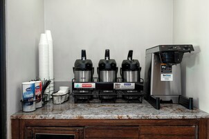 Estação de café com três máquinas de café, um dispensador de água quente e uma pilha de copos brancos.