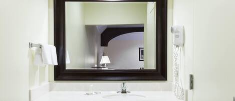 Casa de banho com uma pia branca, um espelho com moldura escura, um porta-toalhas e um secador de cabelo preso à parede.