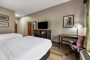 Quarto de hotel com duas camas, uma escrivaninha com cadeira, televisão e luminária.