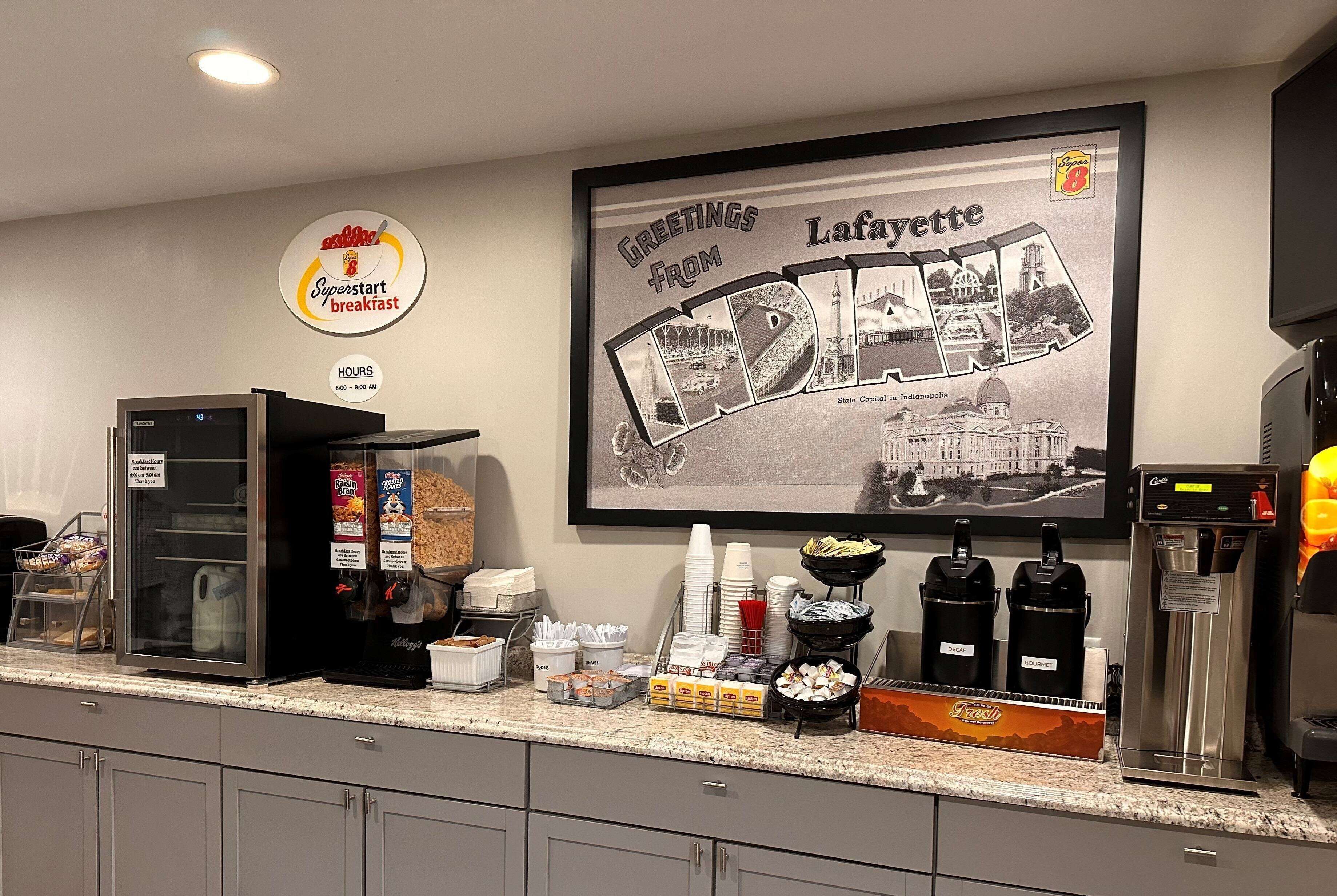 Espaço de buffet de café da manhã com um letreiro Superstart, um letreiro de boas-vindas emoldurado para Lafayette, Indiana, e diversos dispensadores de alimentos e bebidas.