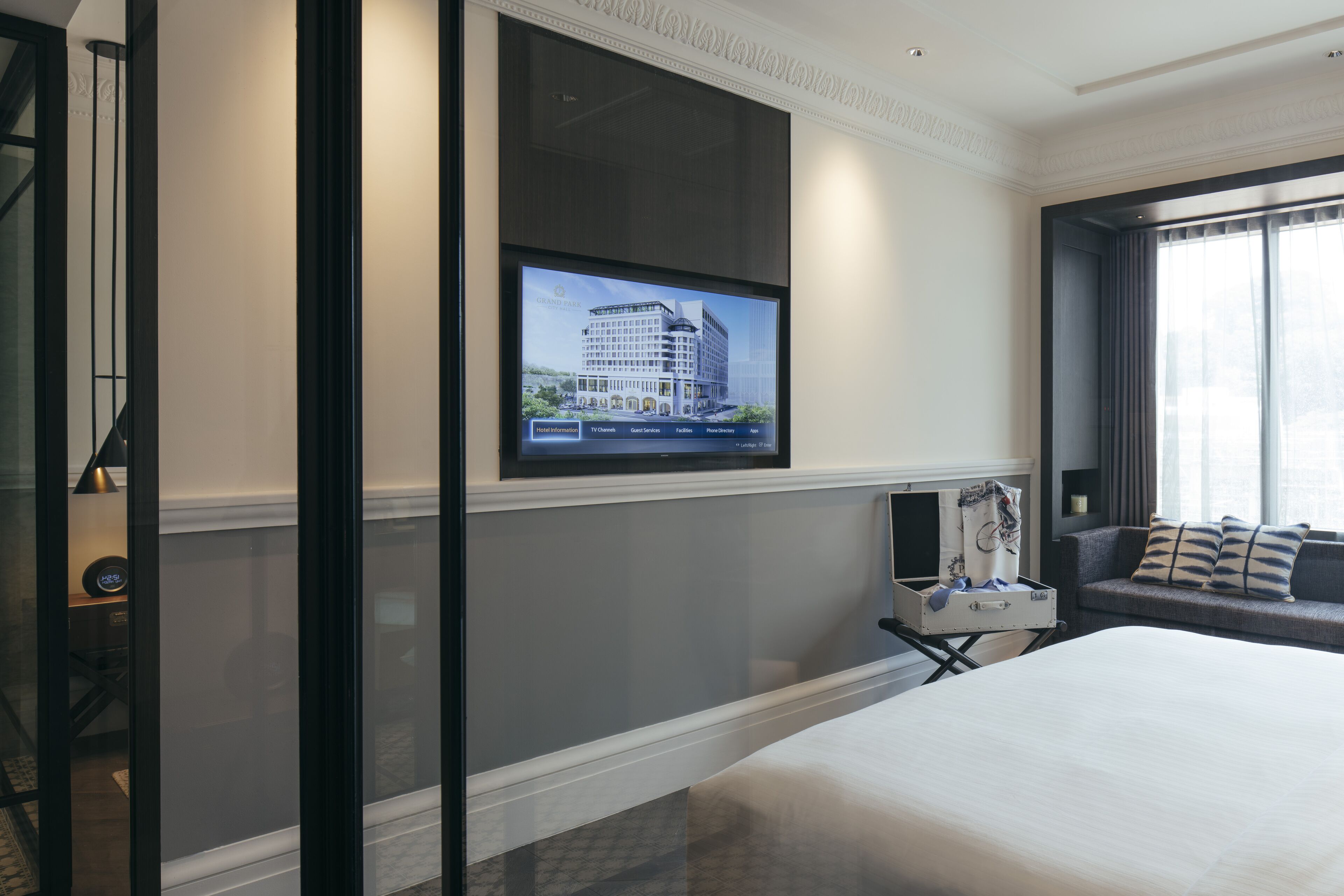 Quarto de hotel com uma cama grande, televisão fixada na parede, janela com cortinas e uma pequena mesa com abajur.