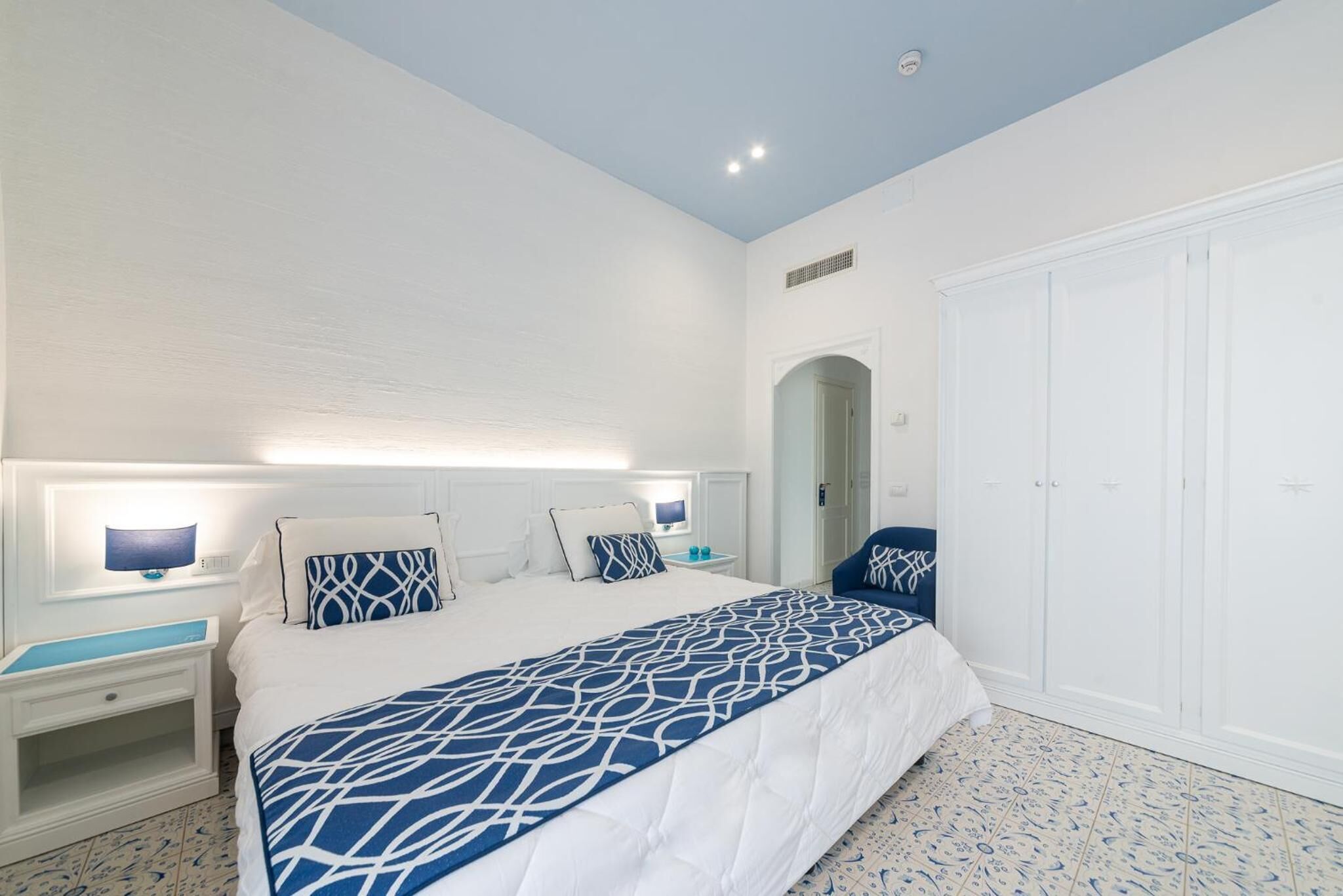 Quarto de hotel com uma cama grande, paredes brancas, teto azul e um guarda-roupa.