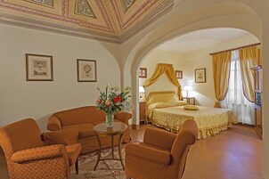 Quarto de hotel com cama, área de estar com cadeiras, uma mesinha e um vaso de flores.