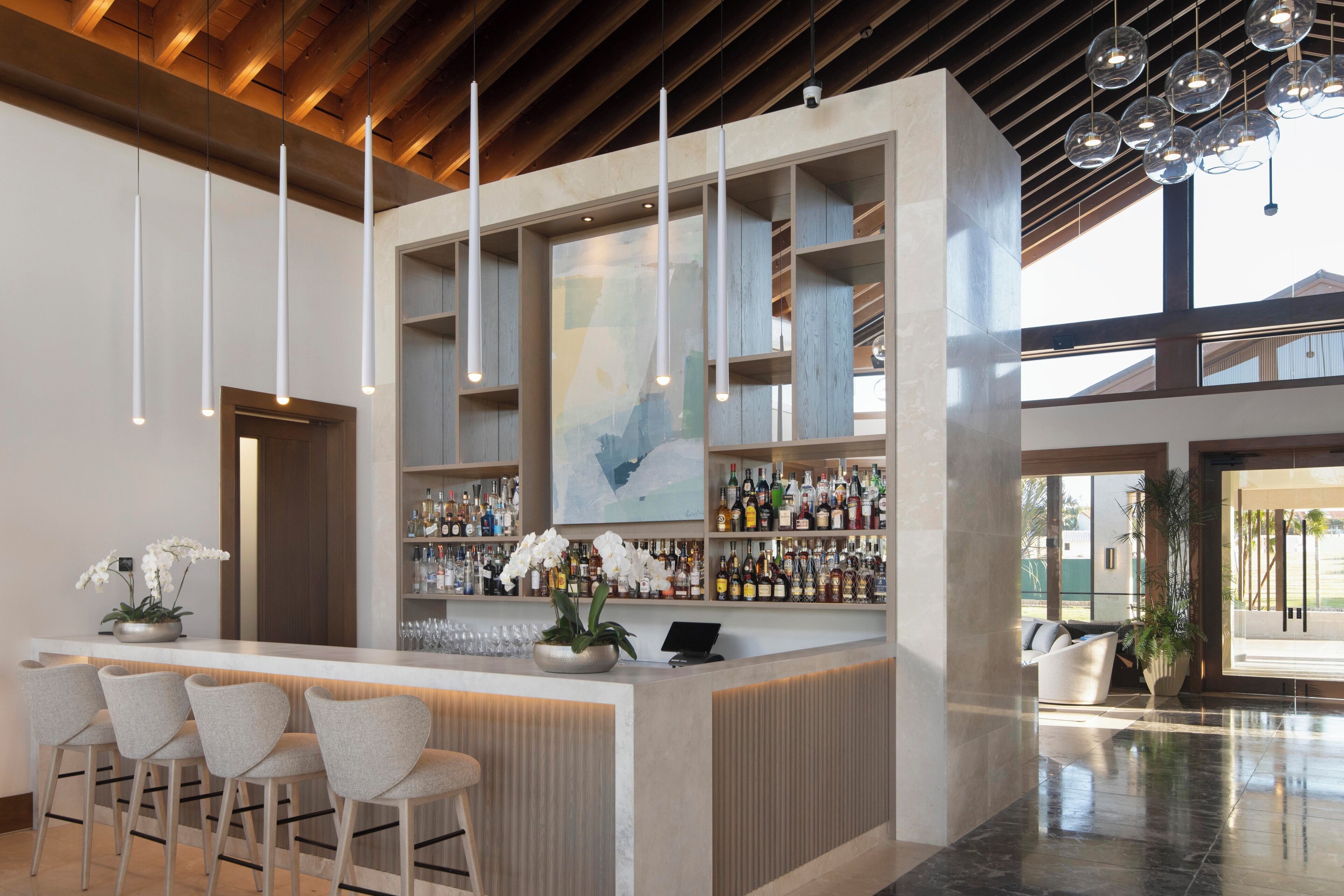 Uma área de bar moderna com um balcão central, banquetas e uma variedade de garrafas.