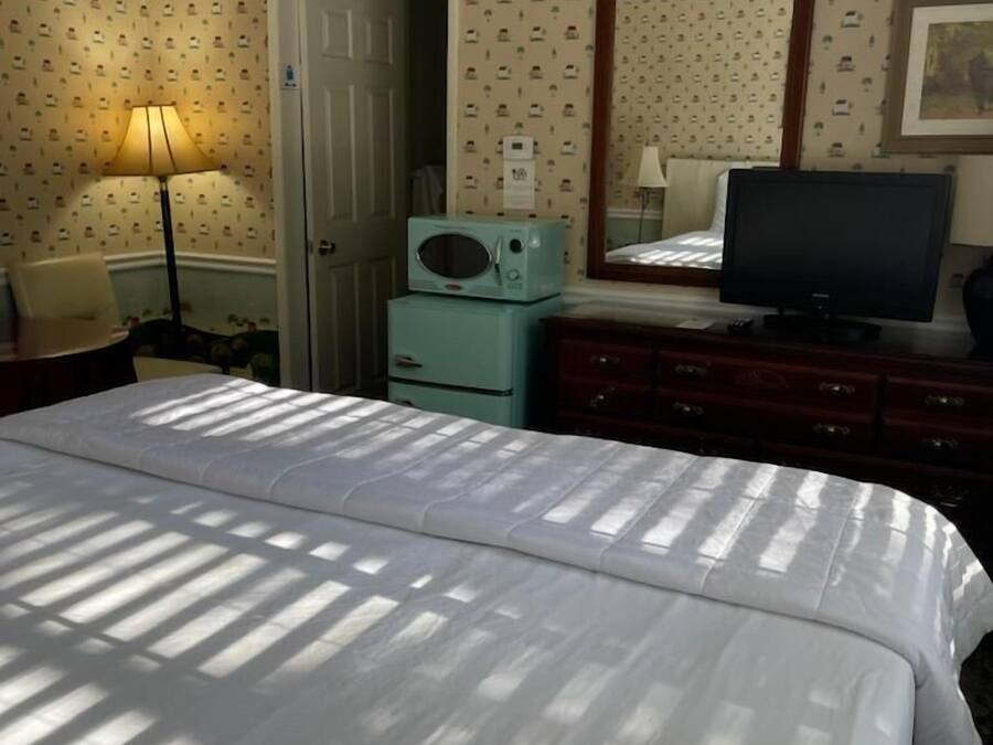 Quarto de hotel com uma cama grande, televisão, cómoda, micro-ondas e porta que dá para outro espaço.