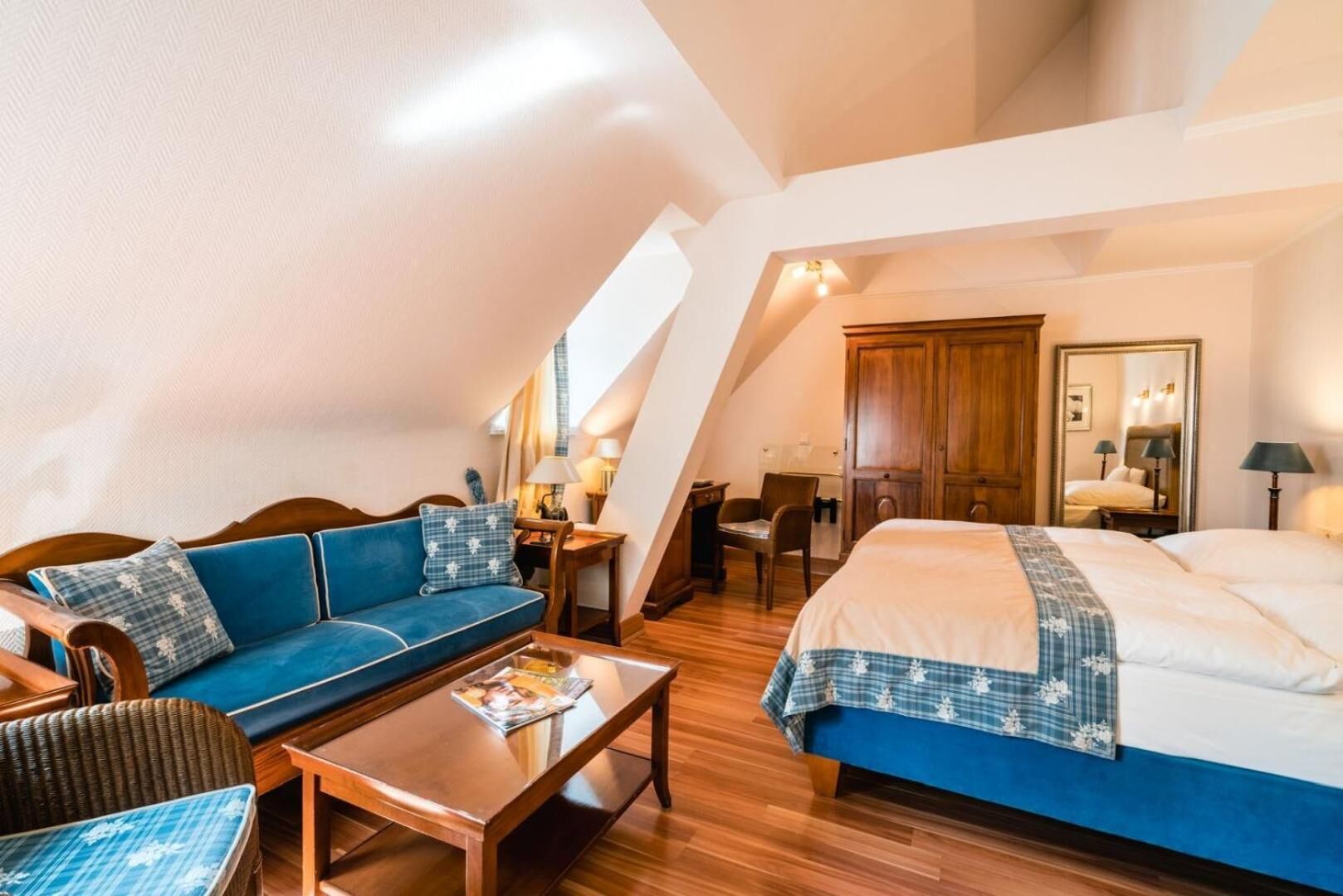Um quarto acolhedor com um sofá azul, uma mesa de centro de madeira, uma cama com colcha azul e branca e um guarda-roupa de madeira.