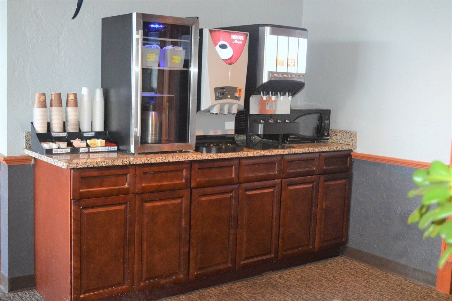 Uma estação de café com serviço próprio, incluindo uma máquina de café, um dispensador de bebidas e um refrigerador com produtos.
