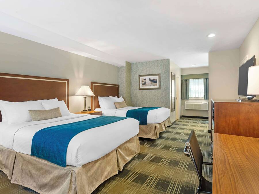 Quarto de hotel com duas camas, uma mesa, uma cadeira, uma televisão e um quadro na parede.