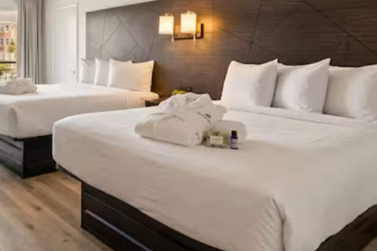 Quarto de hotel com duas camas, cabeceira escura e mesa de cabeceira com artigos de higiene pessoal.