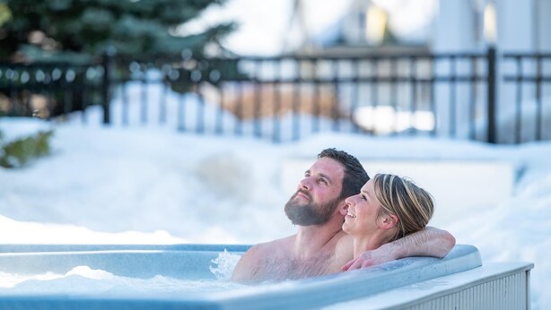 Um casal em uma banheira de hidromassagem rodeado por neve.