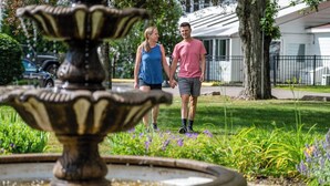 Uma fonte num jardim com um casal caminhando perto.