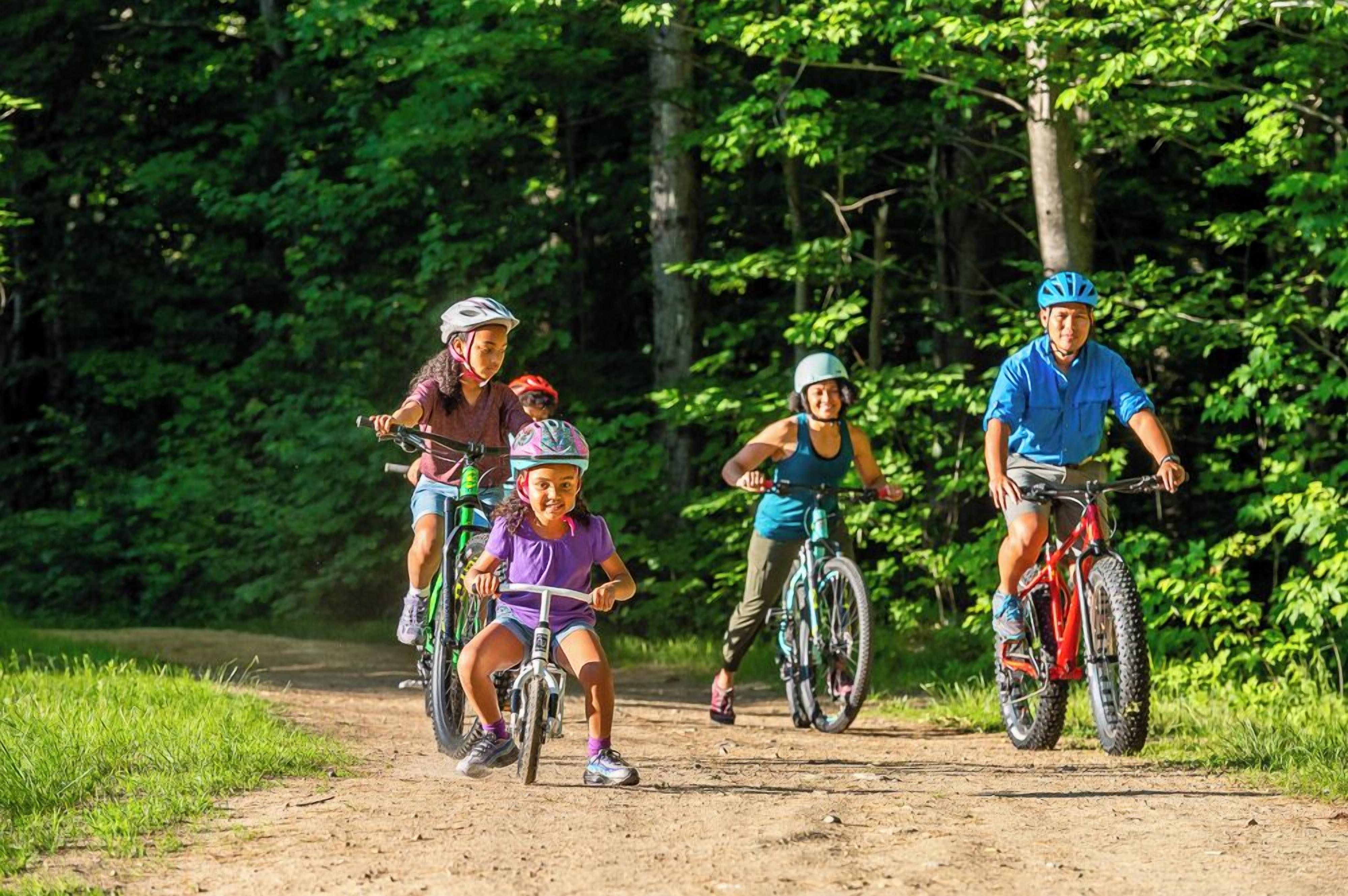 Um grupo de pessoas andando de bicicleta por uma trilha de terra cercada por árvores.